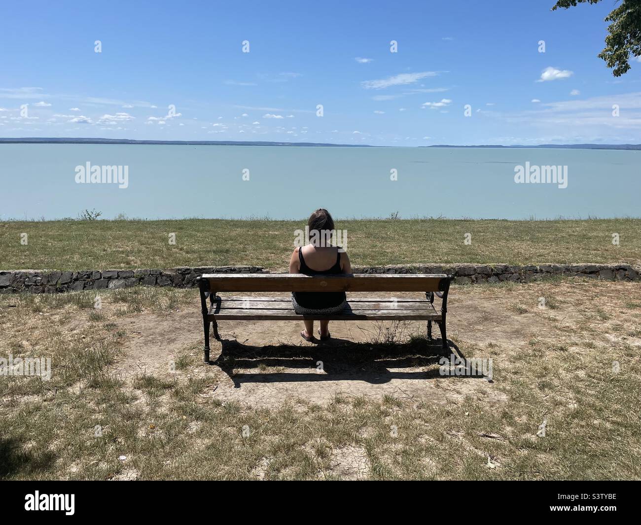 Girl sitting alone on a bench staring at a lake Stock Photo - Alamy