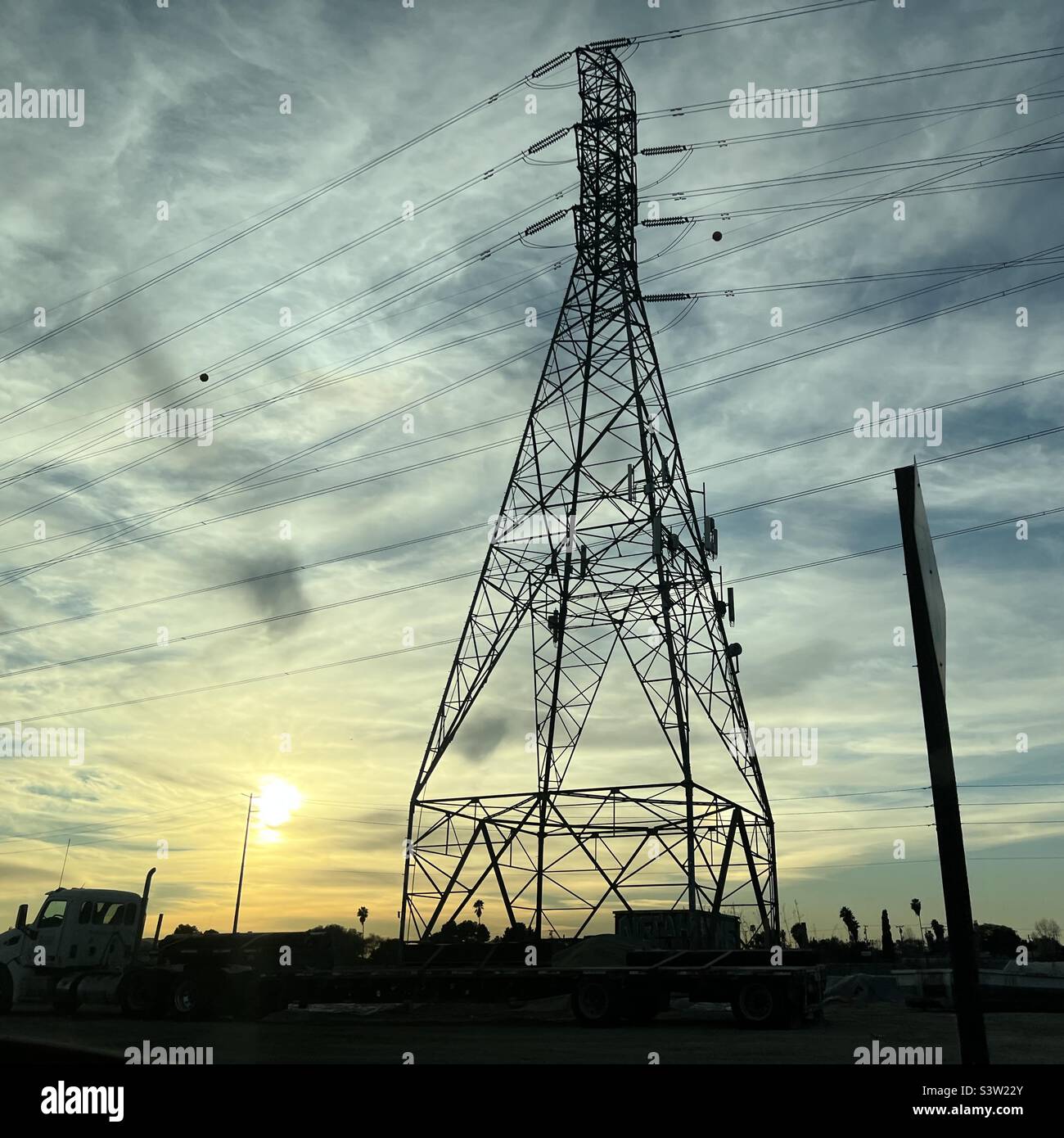 Silhouetted electricity pylon with dramatic cyan sky and low, golden ...