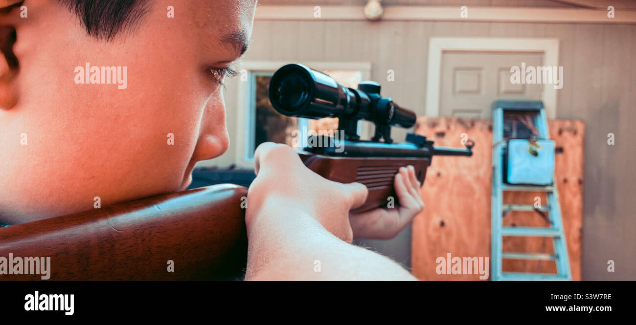 A boy looking down the sights, aiming an air rifle at a target on some ...
