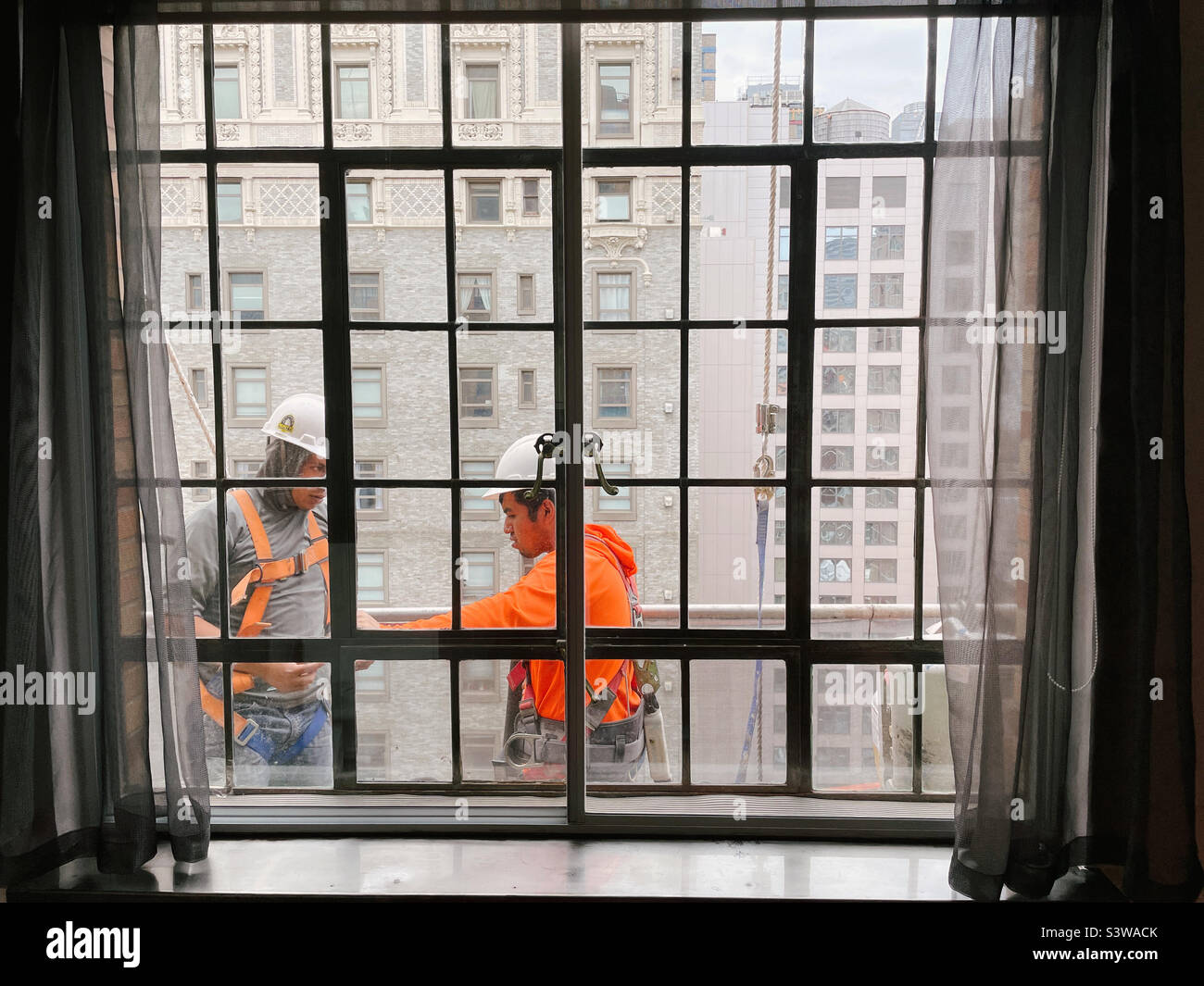Workers outside an apartment casement window applying waterproofing ...