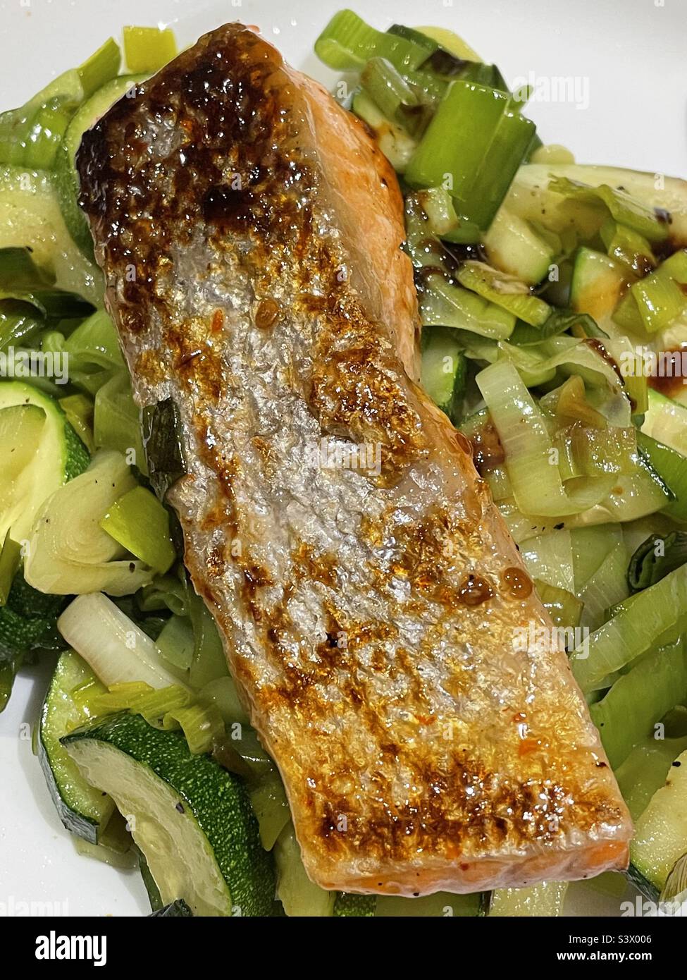Crispy salmon skin on salmon fish fillet on bed of sautéed sliced ...