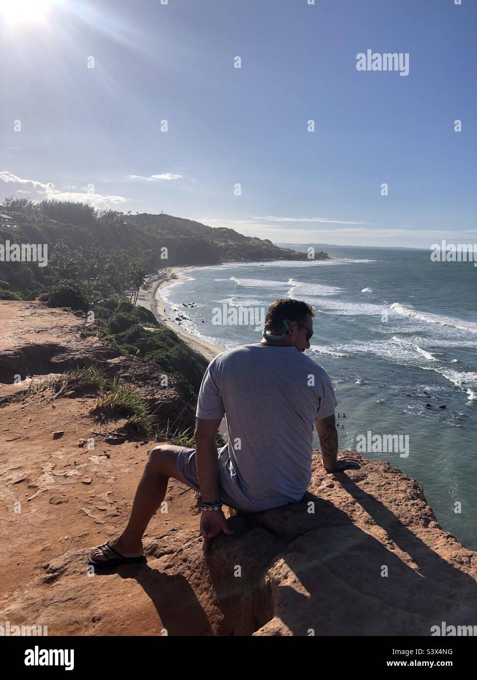 A man sitting on a cliff looking down into the sea Stock Photo - Alamy