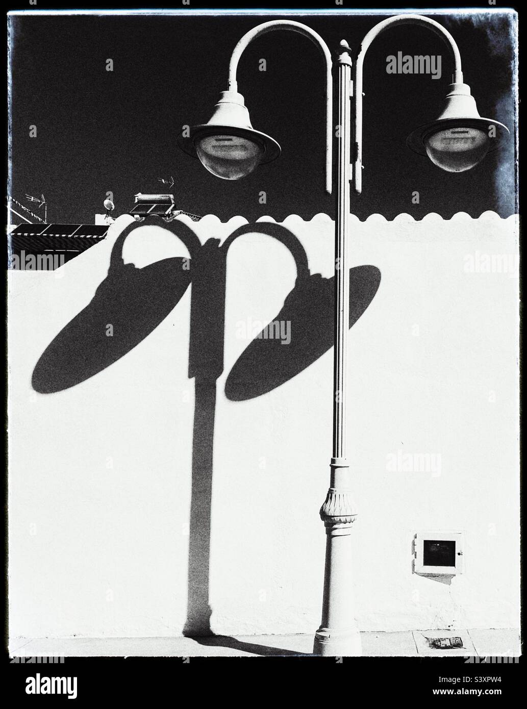 Bright sunlight casts a dark shadow of street lamps onto a white wall ...