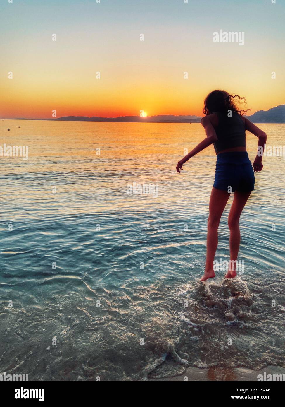 Girl in silhouette jumping in sea at sunset. Pefkos beach on island of ...