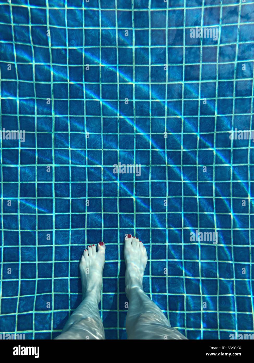Looking down on a woman’s feet and legs with red painted toenails in a ...