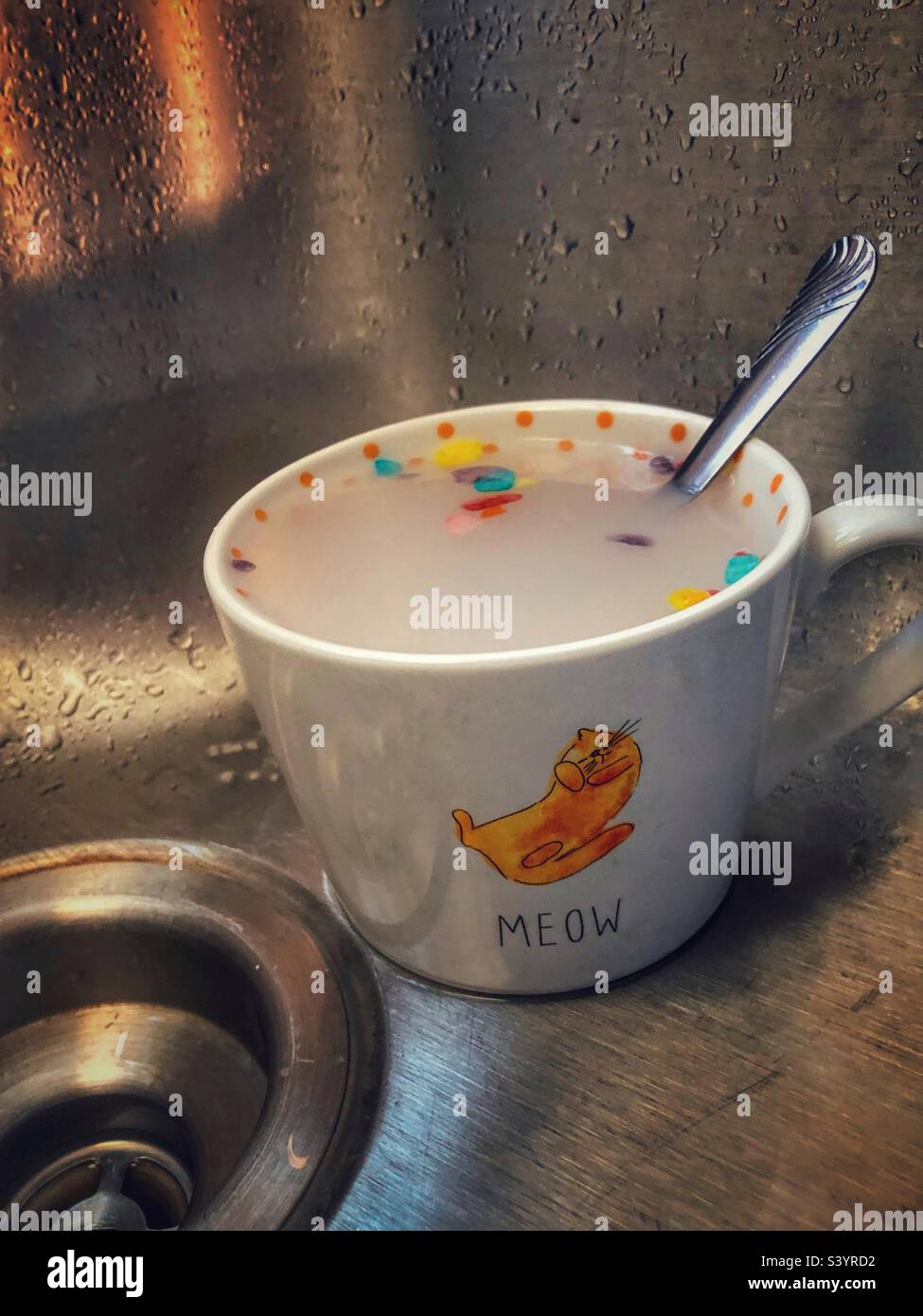 Kitty mug with colorful cereal set to rinse in a stainless steel sink ...