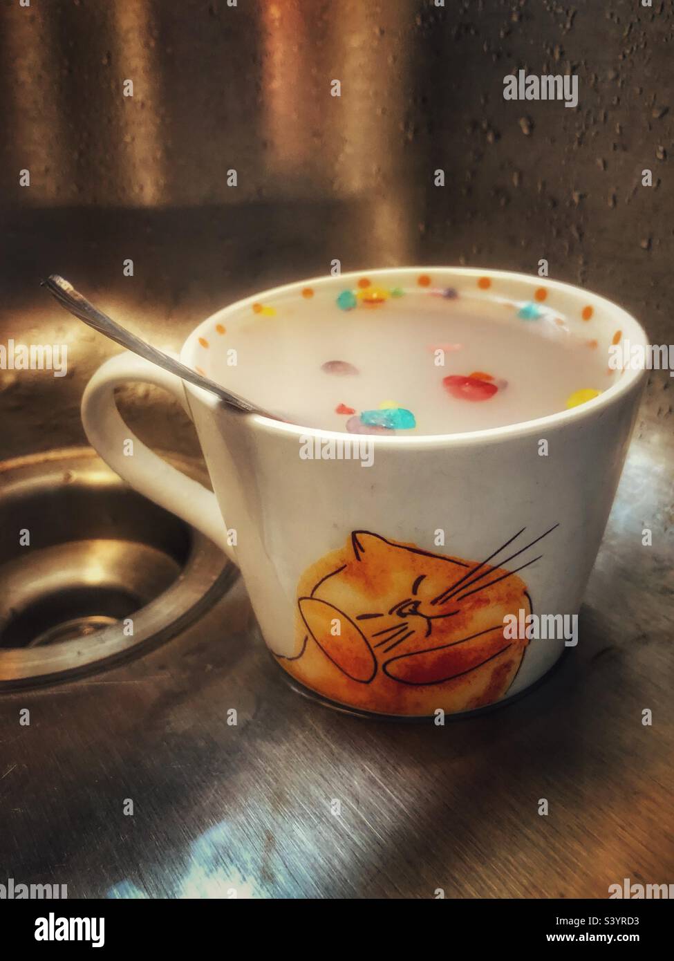 Cute kitty mug of colorful cereal set to rinse on a stainless steel ...