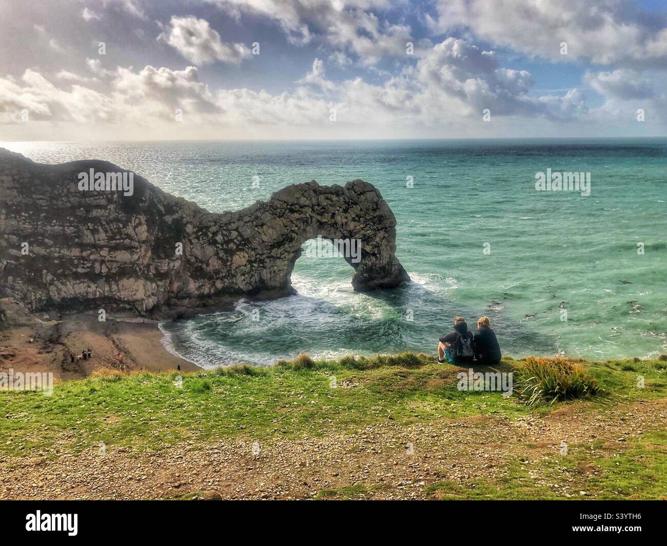 Couple sat on edge of cliffs viewing Durdle Door in Dorset United ...