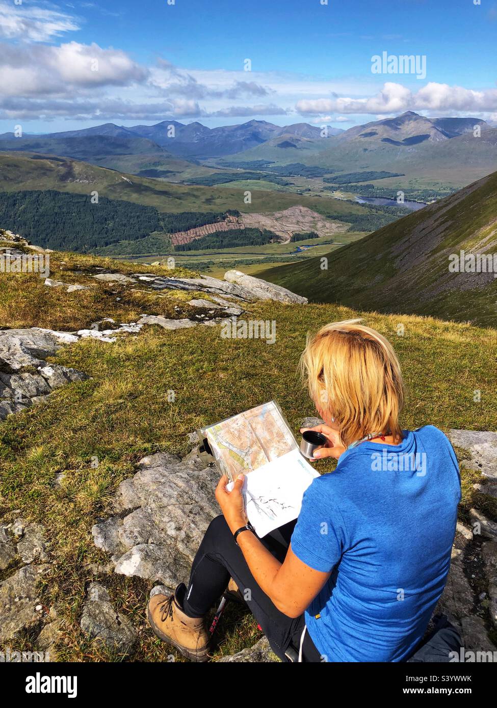 Woman Walker having a break and reading the map on the slopes of Munro ...