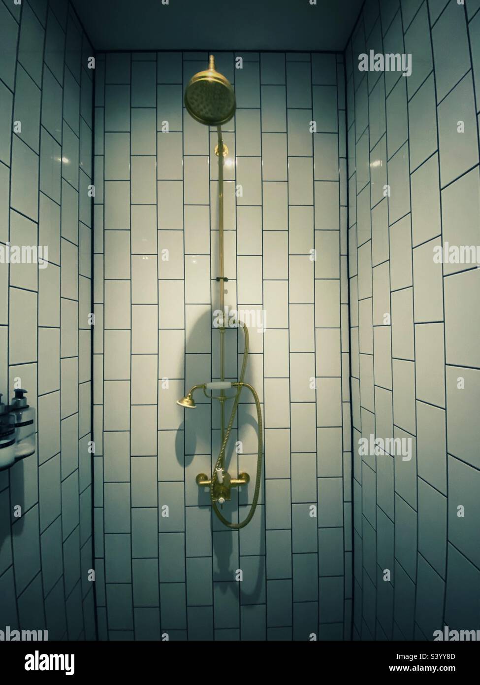 A photograph of a posh-looking brass shower head in a white subway ...