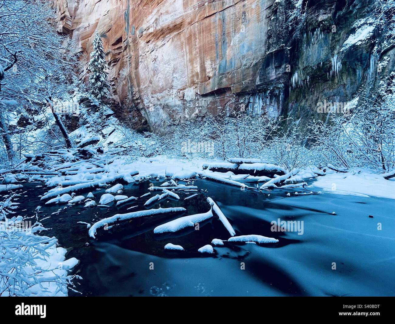 Icy cold frozen stream with snow covered logs in winter wonderland ...