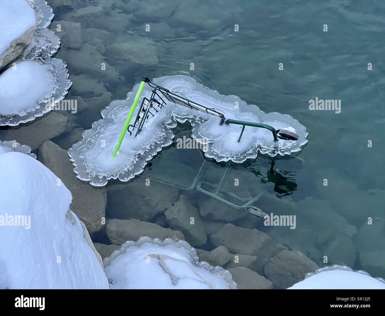 Abandoned shopping cart frozen in curvy ice pattern, lower part showing ...