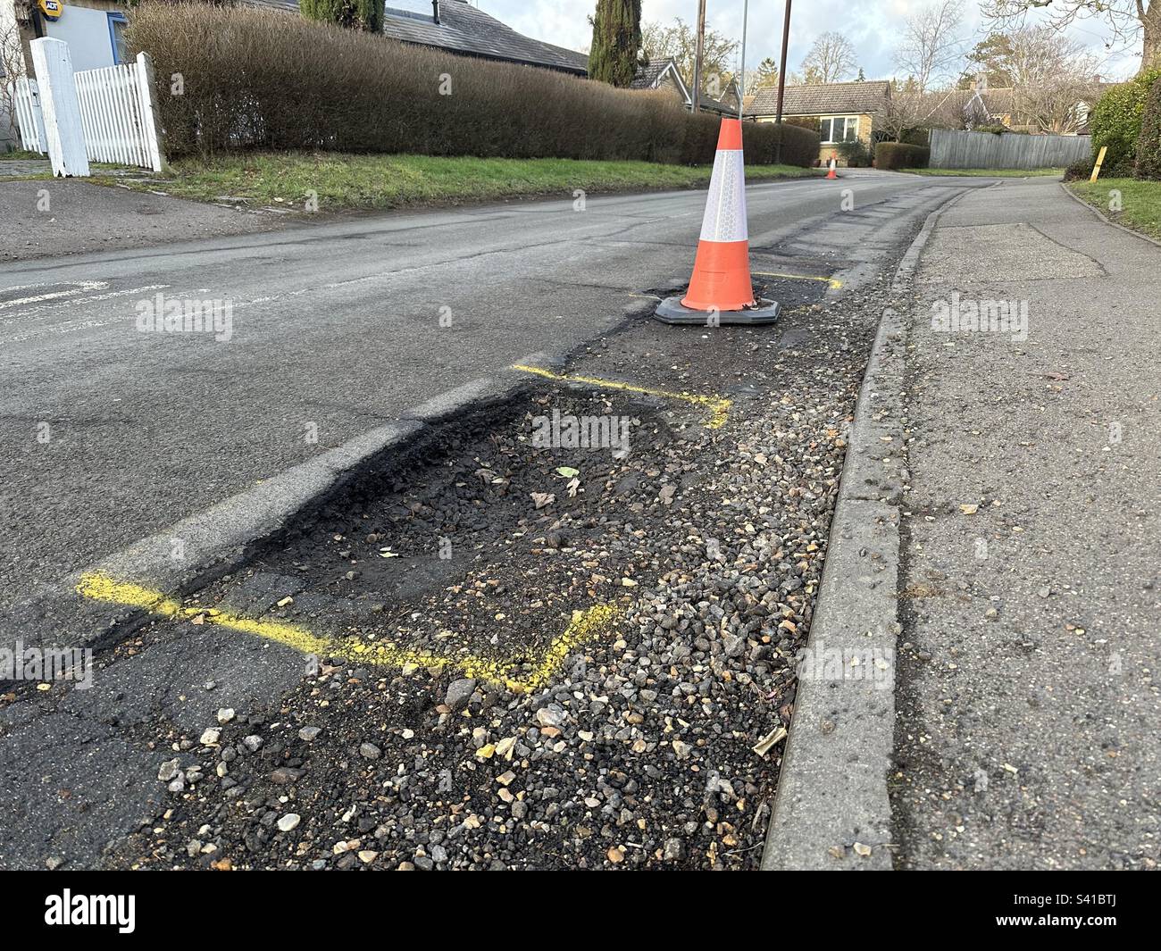 Damaged road with large pot holes marked by traffic cones Stock Photo ...