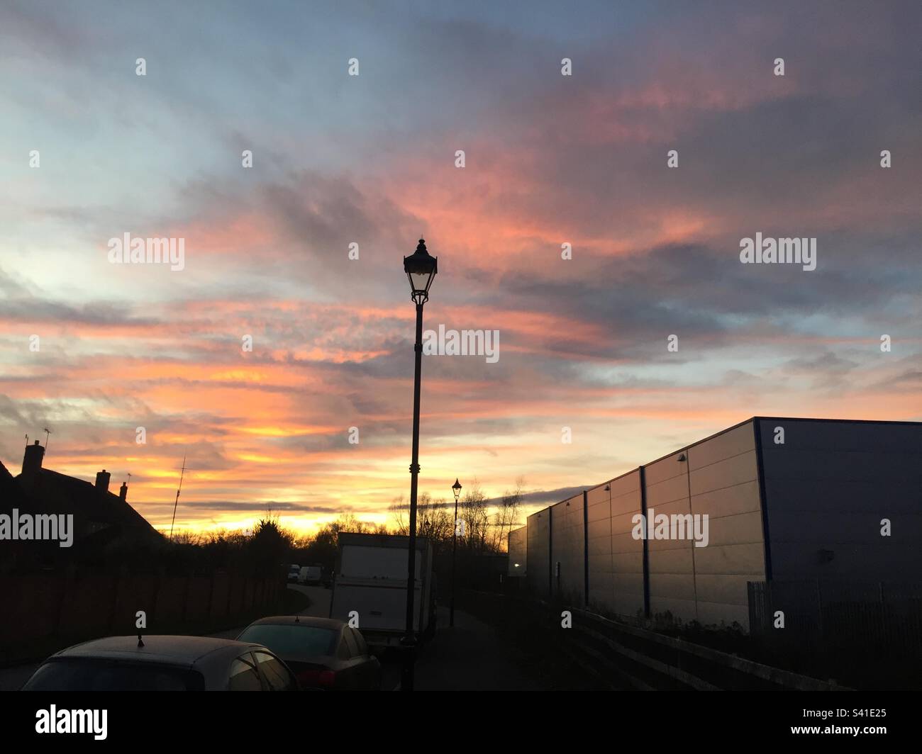 Colourful sunset sky with silhouetted lamp posts trees and rooftops hi ...