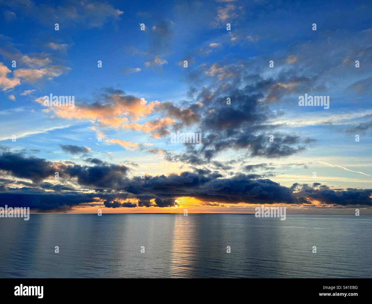 Stunning sunrise landscape horizon over water with low dark clouds and ...