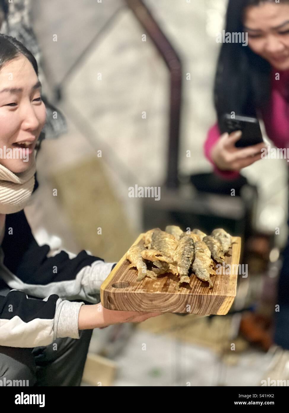 An Asian angler girl holds fried fish on a tray, and another girl takes ...
