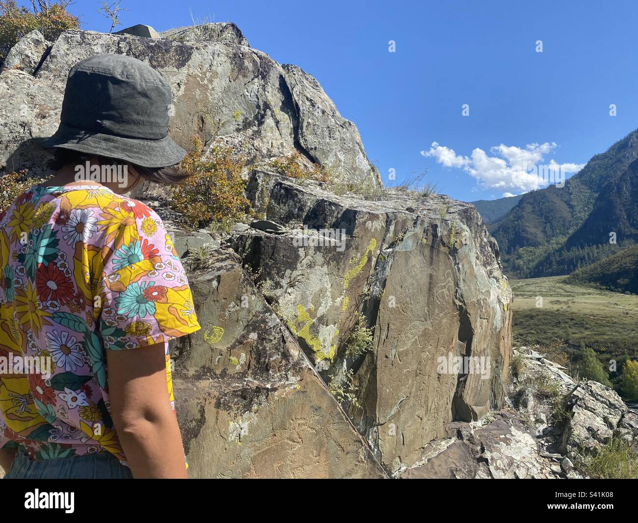 A traveler girl in a hat and a T-shirt with flowers approaches the rock ...
