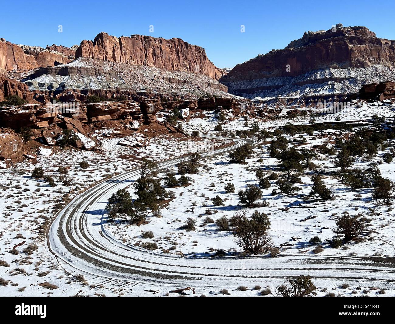 Shot of the snowy road with tire tracks sweeping across with red rocks ...