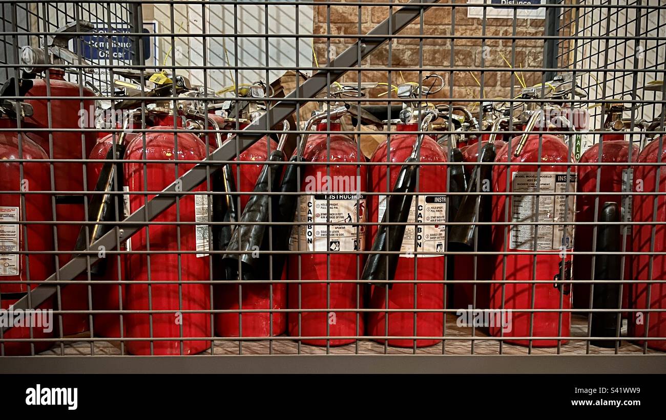 Storage cage containing dozens of bright red fire extinguishers inside ...