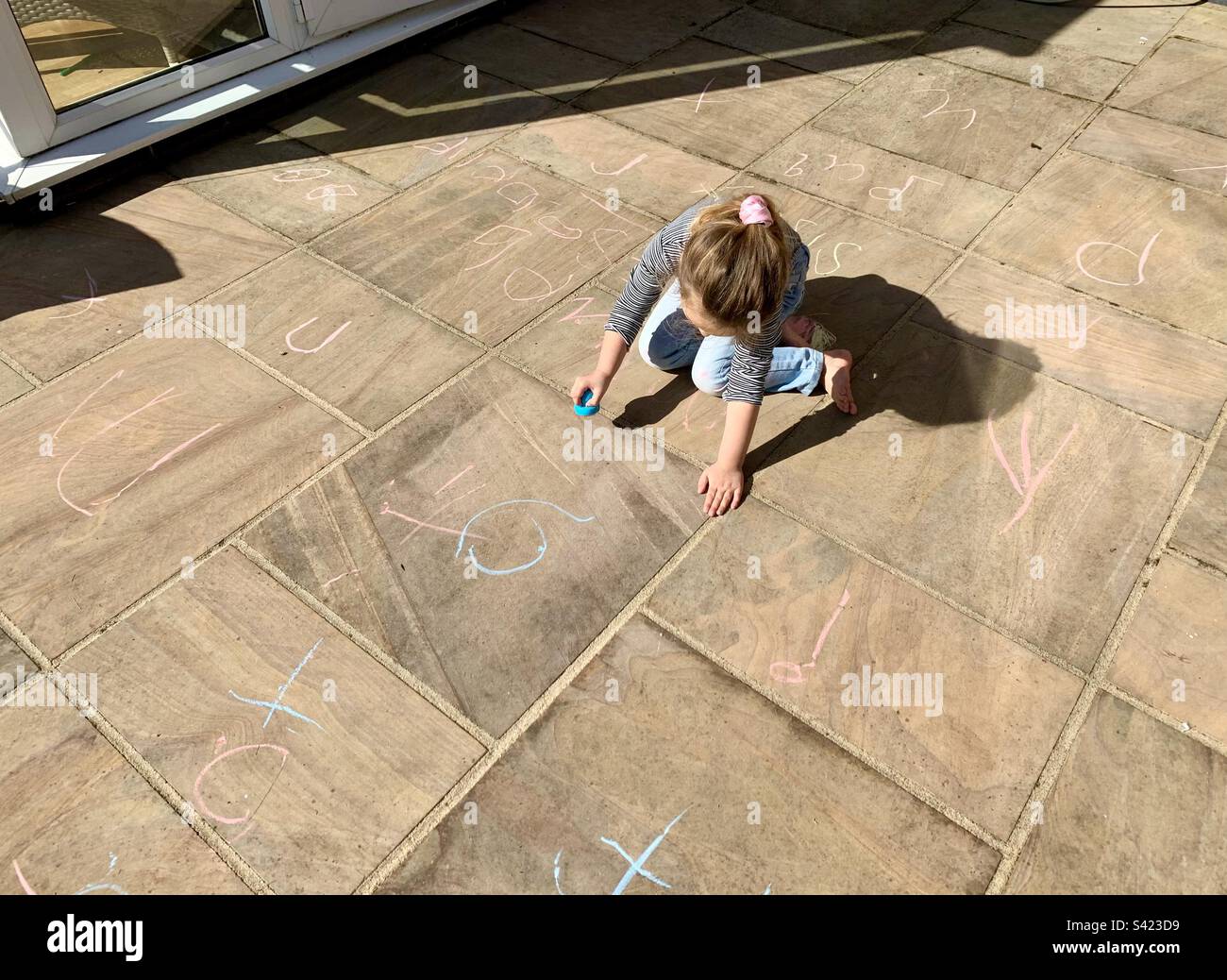 Young child learning her numbers and letters at home, using chalk and ...