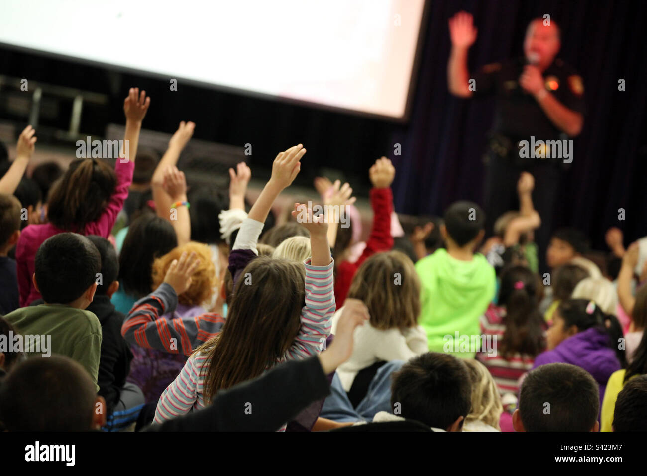 Schoolchildren raising their hands at a school assembly Stock Photo - Alamy
