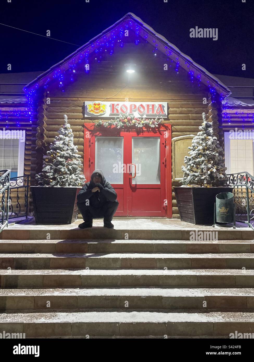 A Russian man is squatting by the stairs of a store at night in winter ...