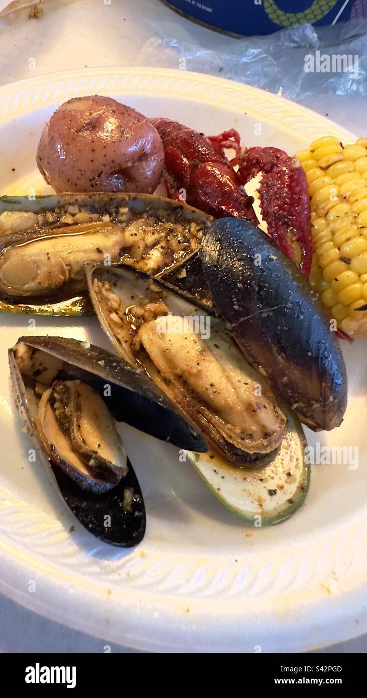 Black and green mussels, with a potato, corn, cob, and crawfish on a ...