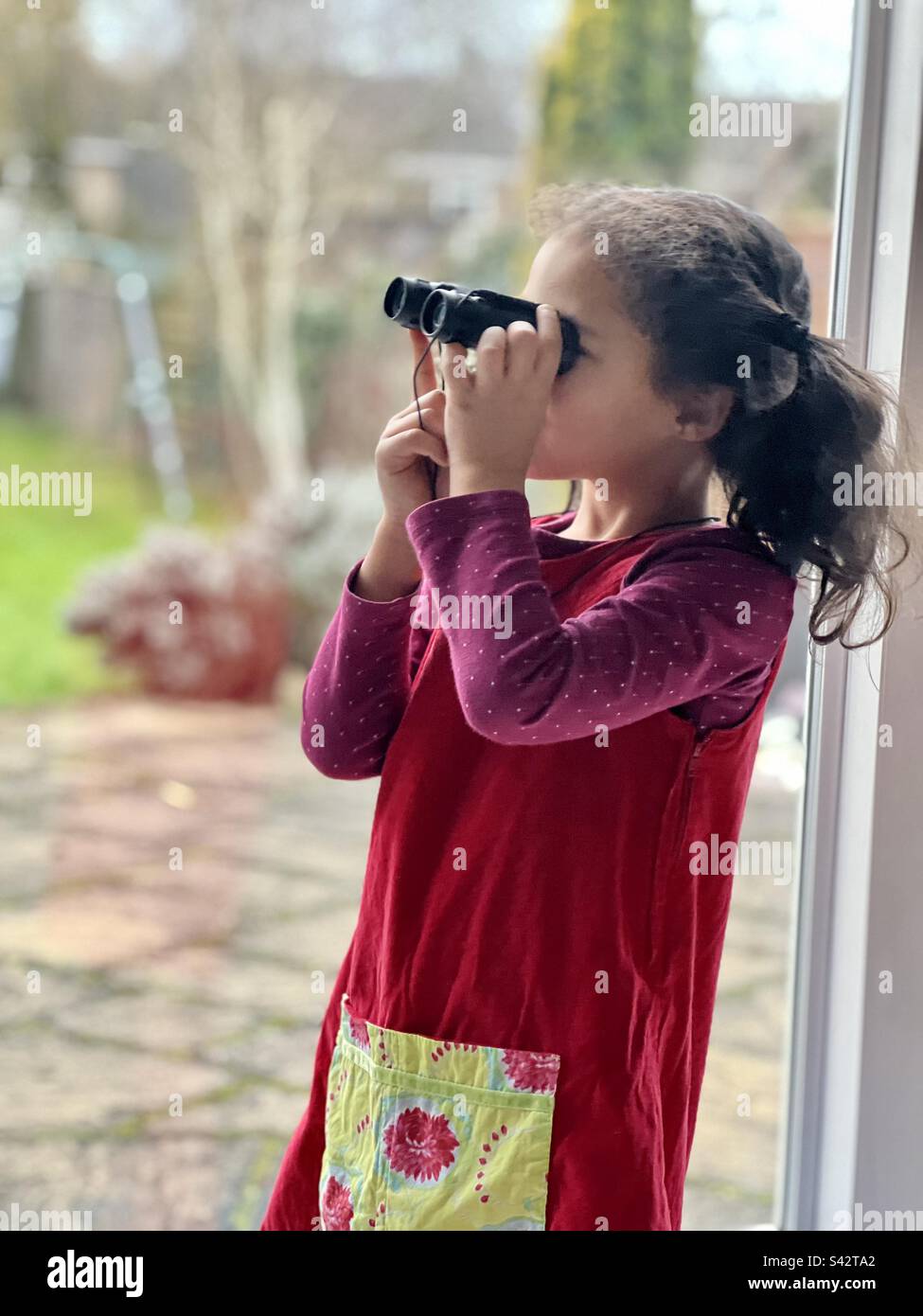 Young girl looking through binoculars out of a window Stock Photo - Alamy