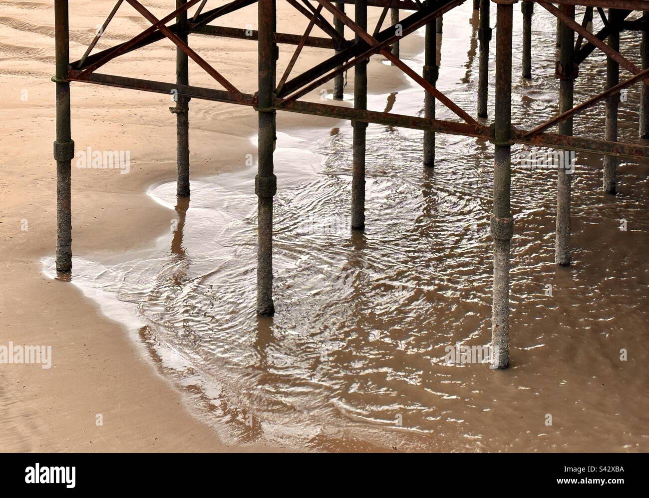 The legs of Blackpool South Pier, in a puddle of seawater, surrounded ...