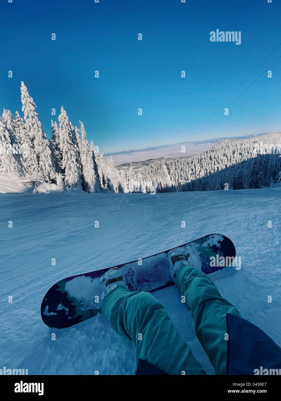 Woman snowbording. Sitting down on the slope, legs and board visible ...