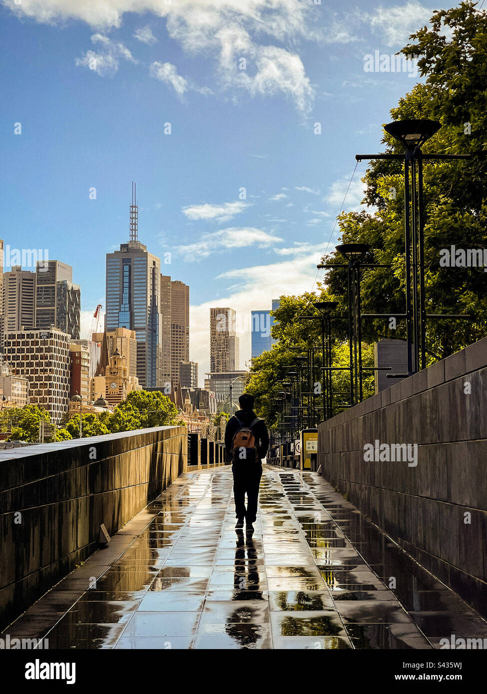 Rear view of man walking on paved footpath against buildings and urban ...