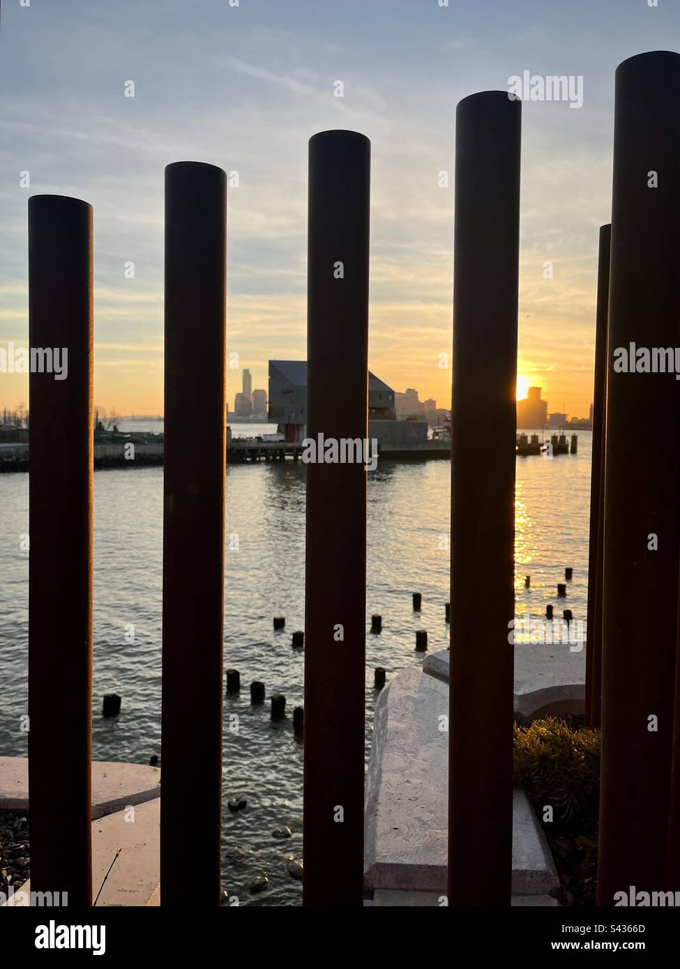 Sunset on Pier 55 seen from the Little Island Park through wooden poles ...