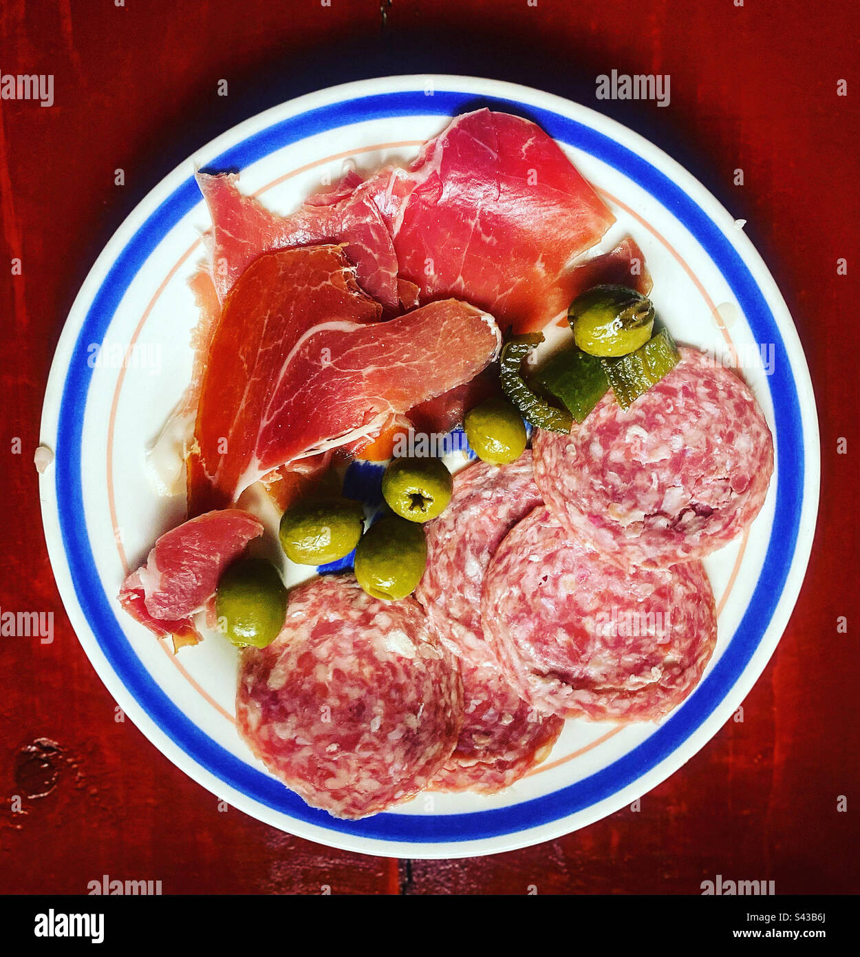 Spanish jamon serrano ham, olives and salami in a plate in a red table ...