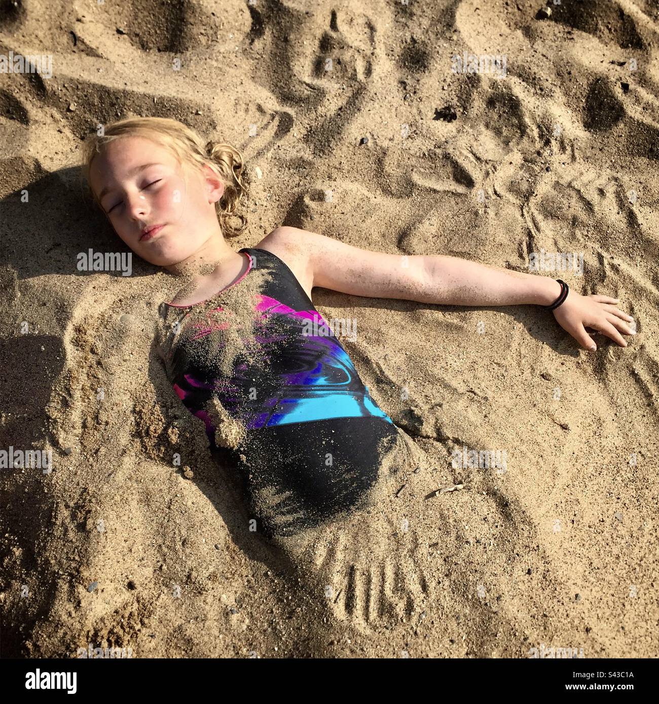 A young girl around eight years old is buried in sand on a beach Stock Photo - Alamy