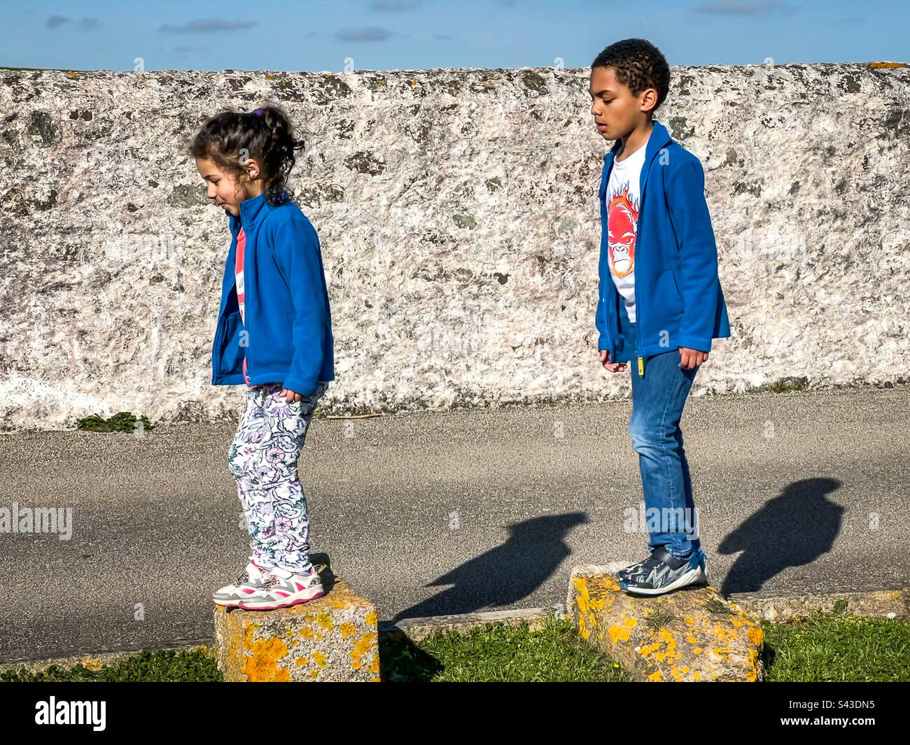 Mixed race brother and sister playing standing on blocks about to jump ...