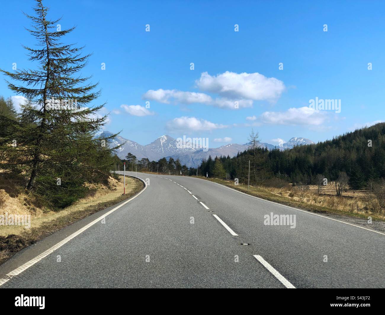 Sweeping A85 road in the Scottish highlands, snow capped peaks and blue ...