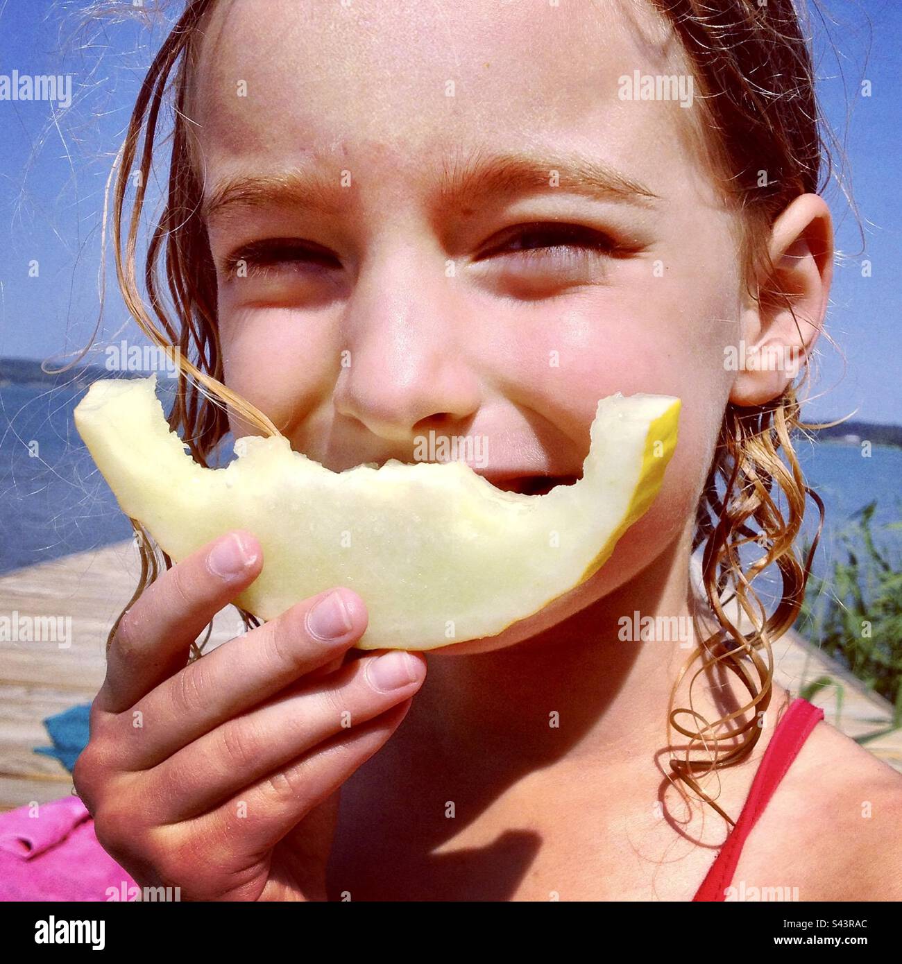 A young 6-year-old girl on holiday pretending to smile using a melon ...