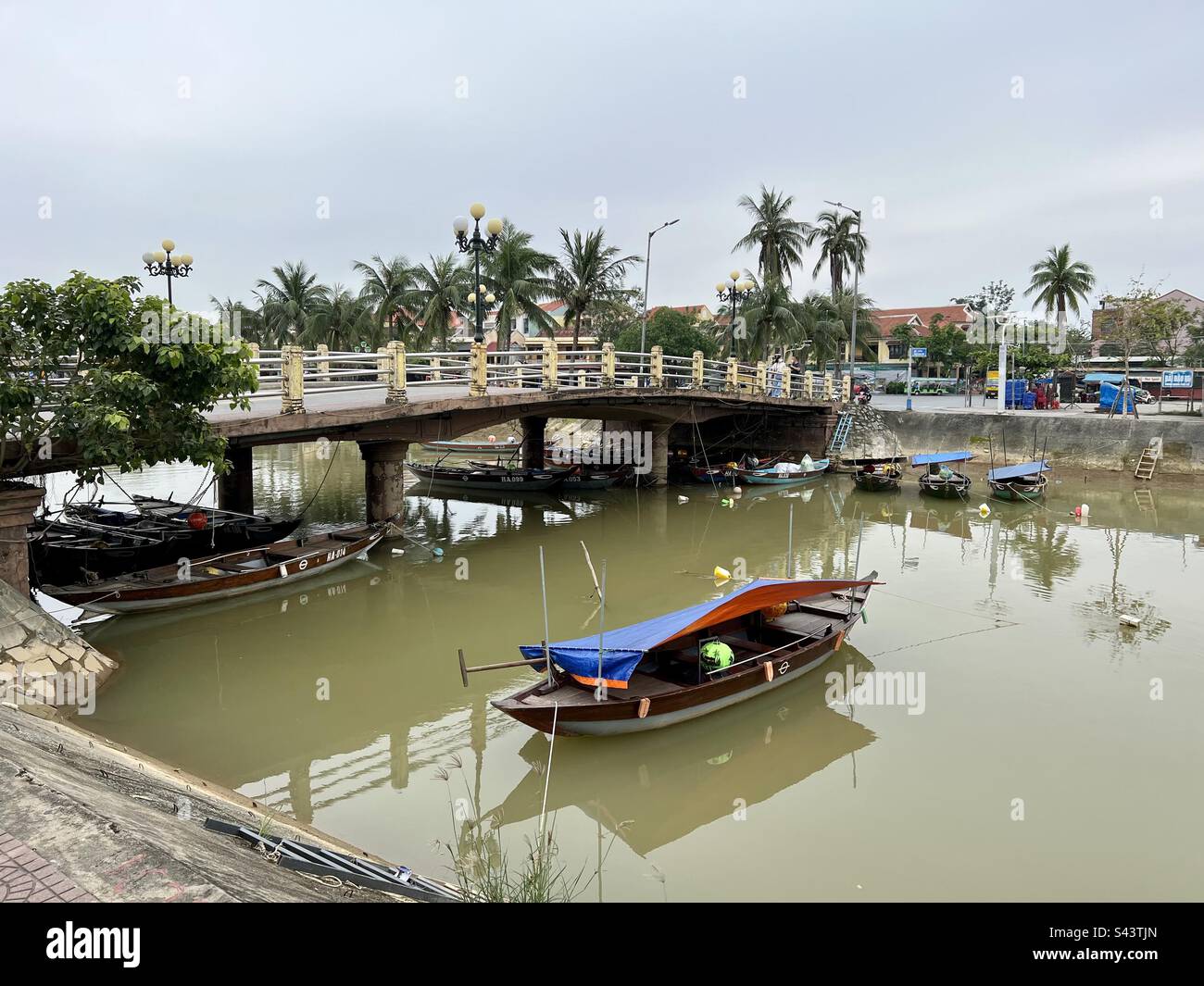 Tiny fishing boats in a small Asian village with a bridge over a river ...