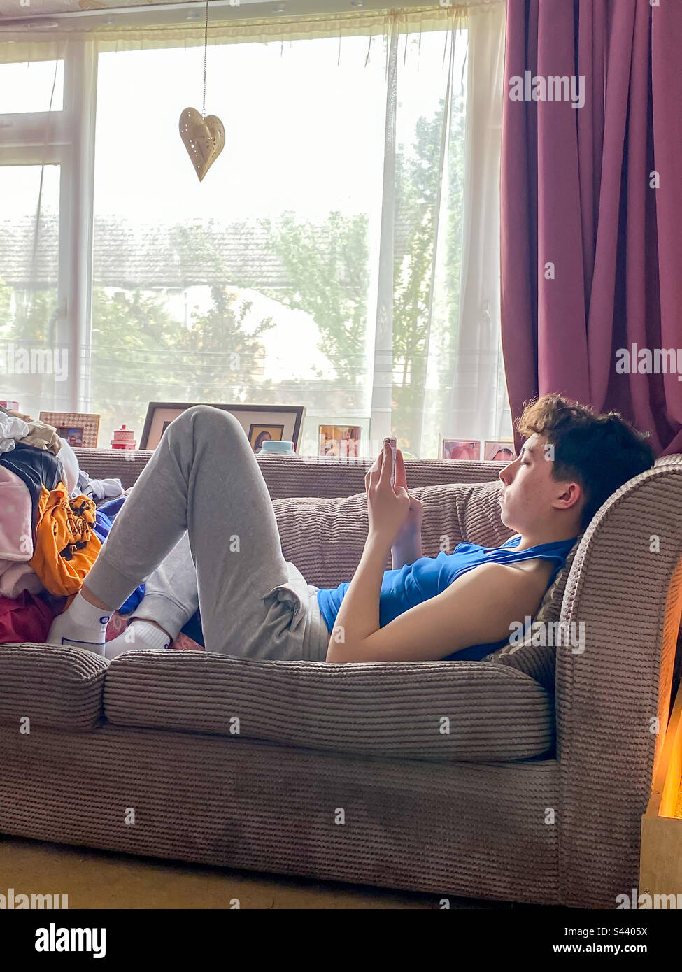 Teenage boy relaxing on a settee in front of a window Stock Photo - Alamy