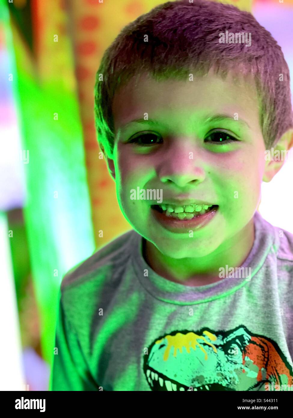 Smiling young boy at a video arcade with green lights reflecting off ...