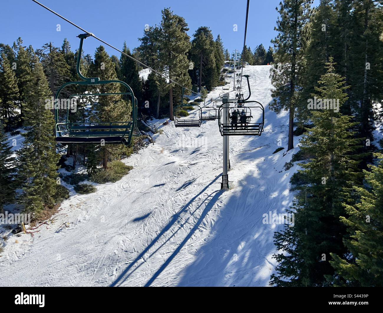 Rear view of unidentified skiers and snowboarders on chairlift going up ...