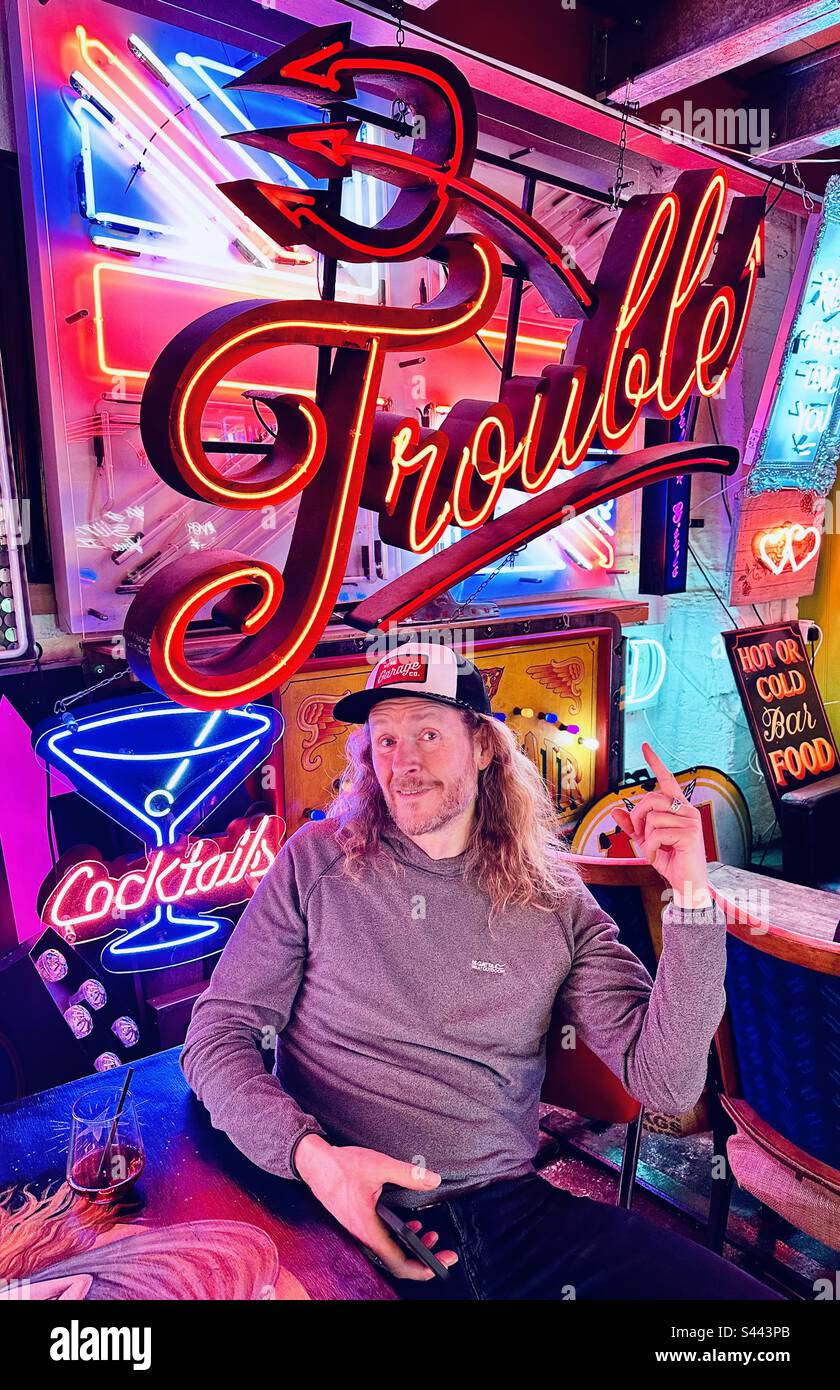 Man in a hat points to a neon Trouble sign in a cafe in London UK Stock ...