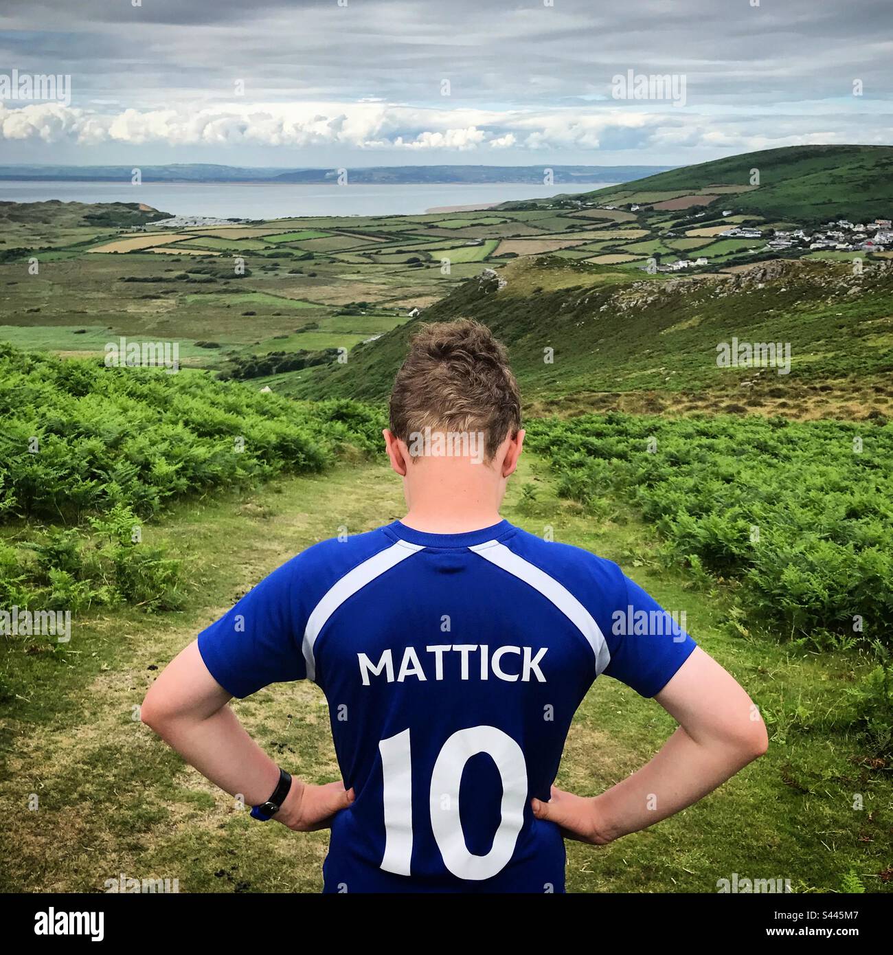 A young 10 year old boy in a football top back to camera hands on hips ...