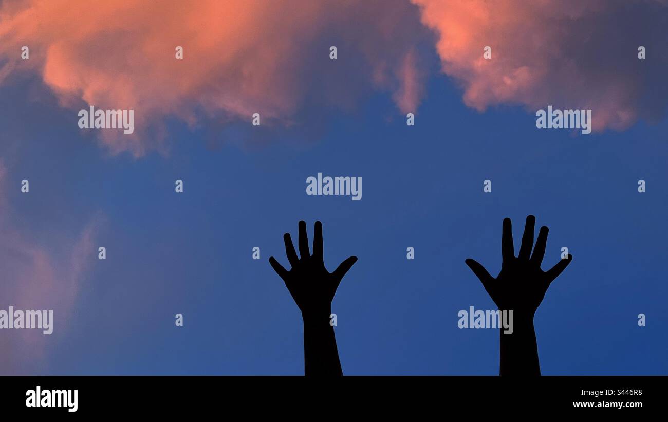 Silhouette of two hands waving out against a cloudy sky background ...