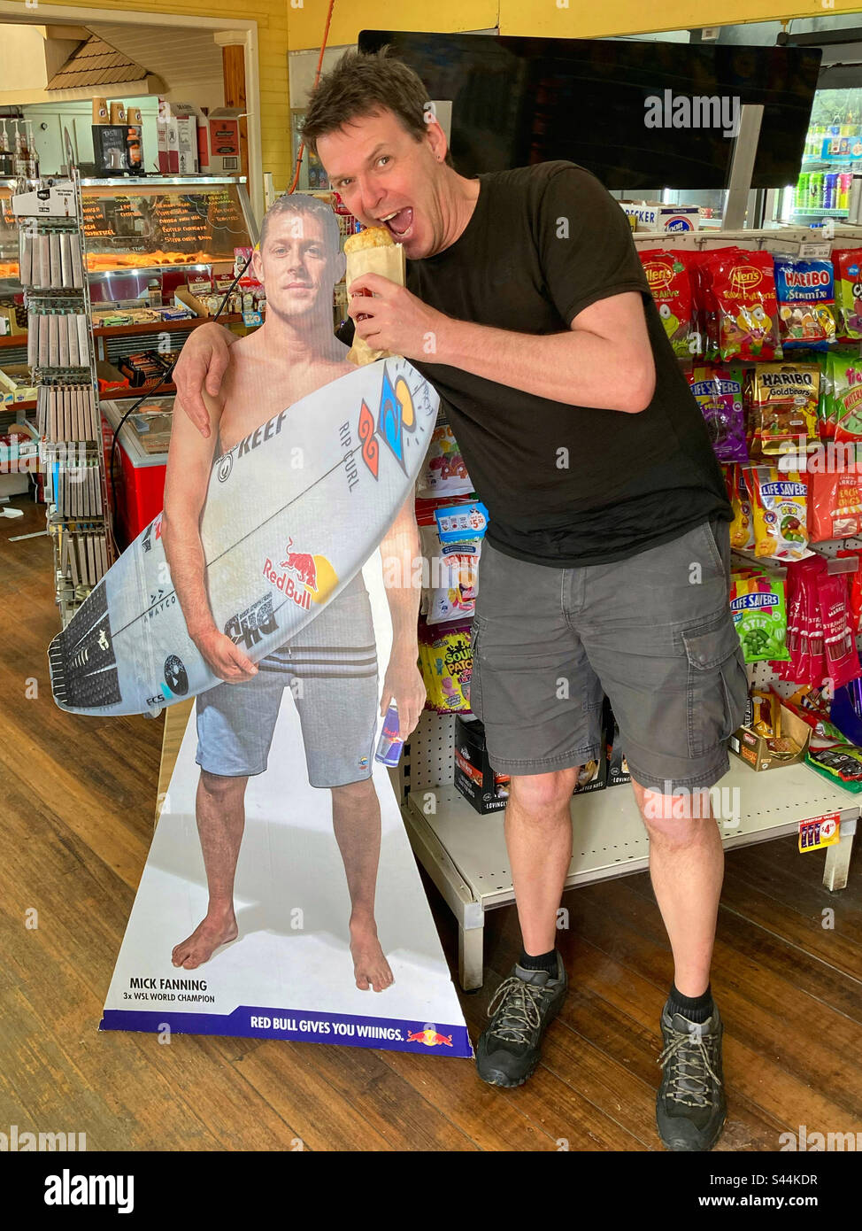 Man eating a snag roll while hanging out with Mick Fanning in a servo ...