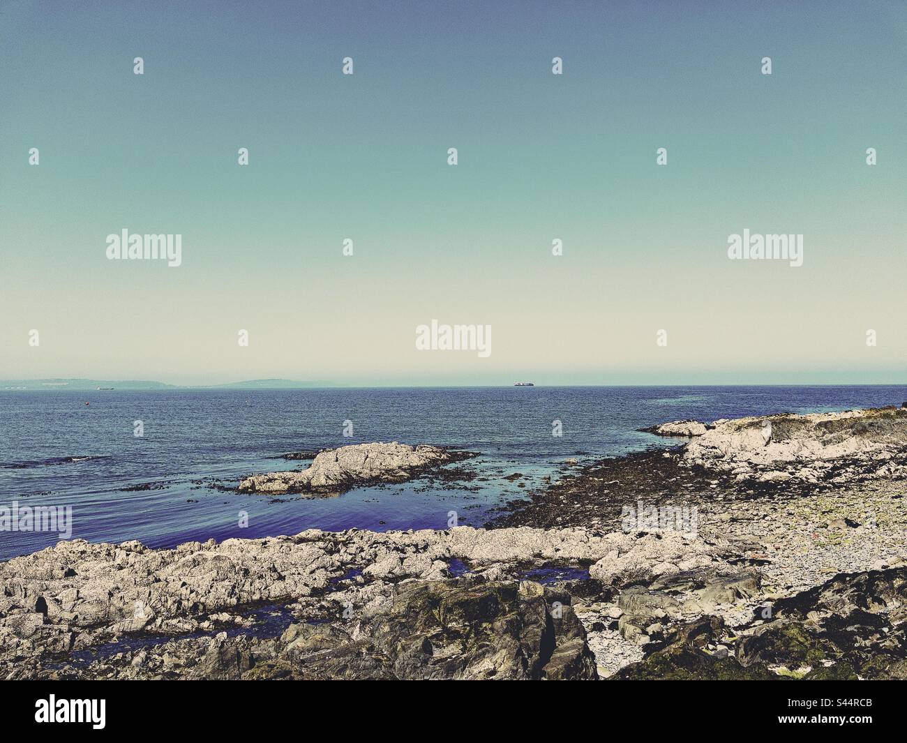 Rocky shore with a ship on the far horizon Stock Photo - Alamy