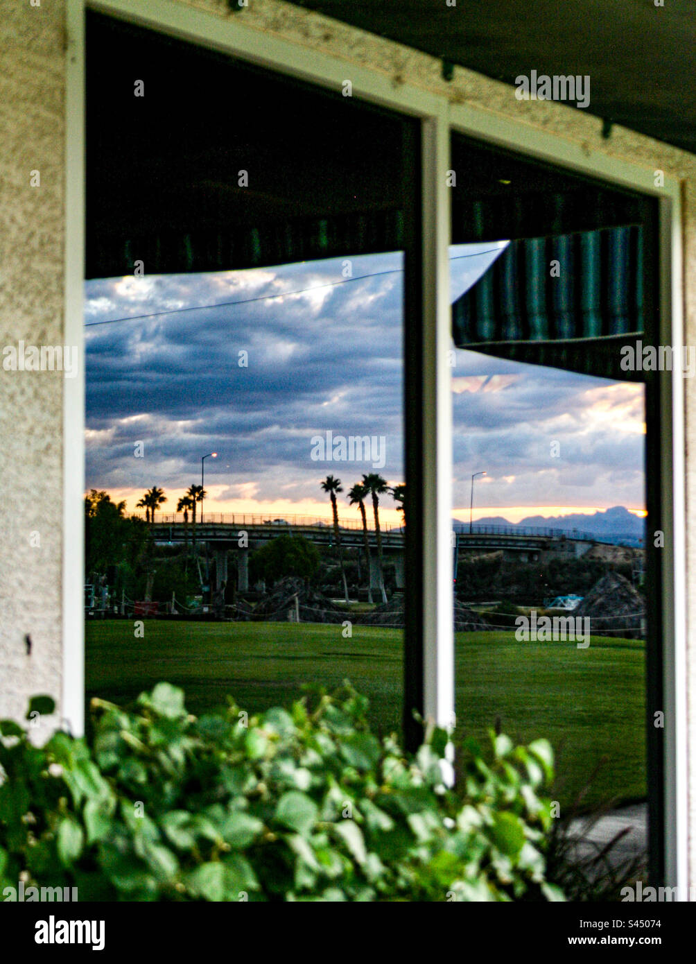 Large window reflection of distant bridge, overcast sky, green grass ...