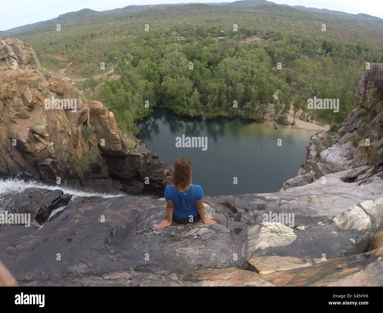 A woman sitting on the edge of the waterfall Gunlom Falls at Kakadu ...