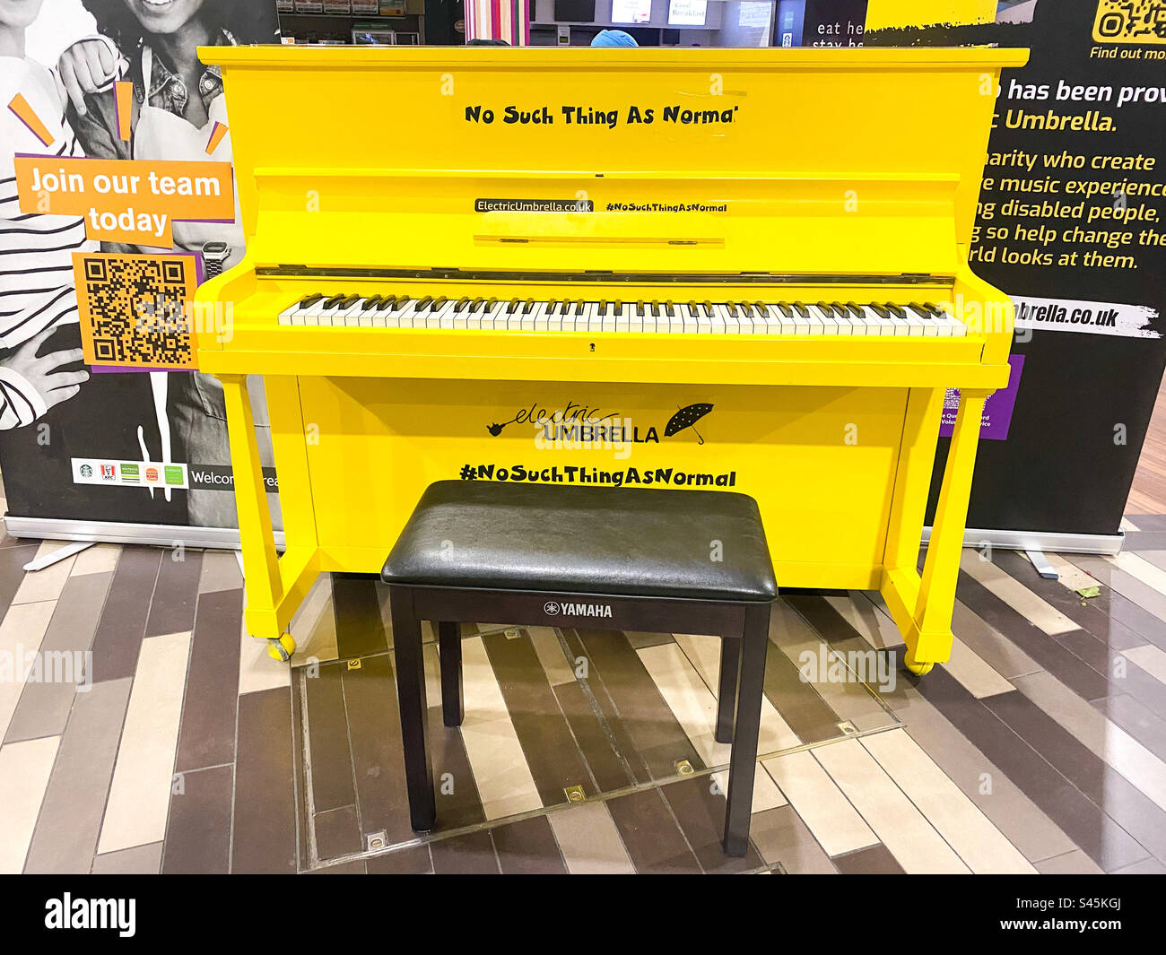 A yellow upright piano for people to play at a motorway service station ...