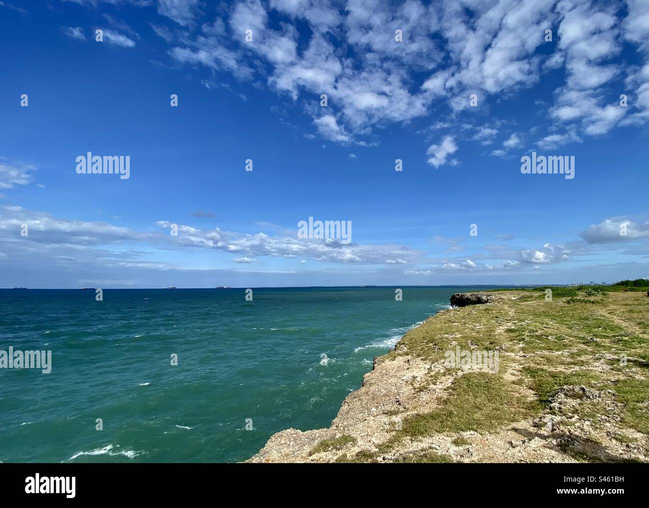 Landscape of sea cliffs with a vibrant blue sky with some fluffy clouds ...
